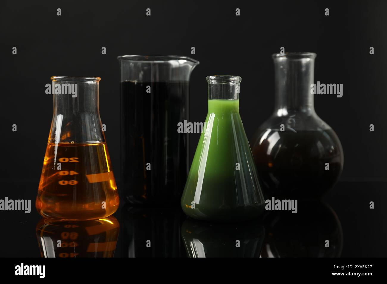 Glass flasks and beaker with different types of oil on black background ...