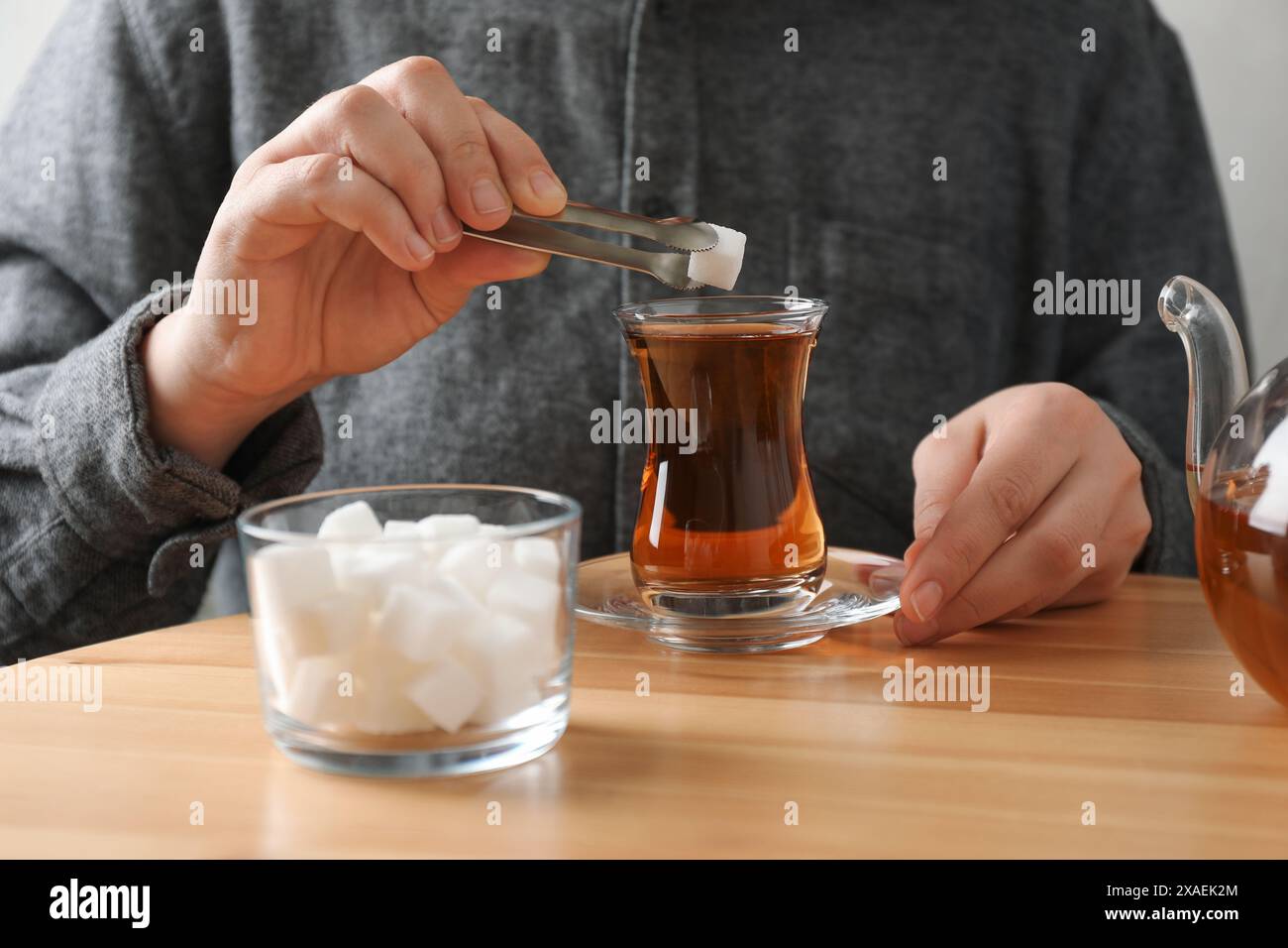 Woman adding sugar cube into aromatic tea at wooden table, closeup ...