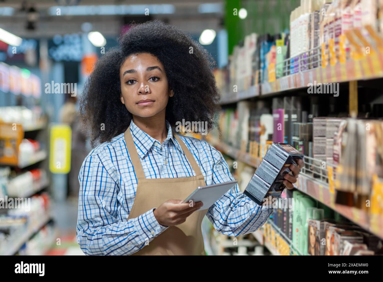 Female store worker in a supermarket aisle holding a digital tablet and ...