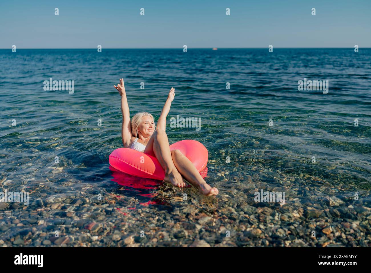 A woman is floating on a pink inflatable raft in the ocean. She is ...