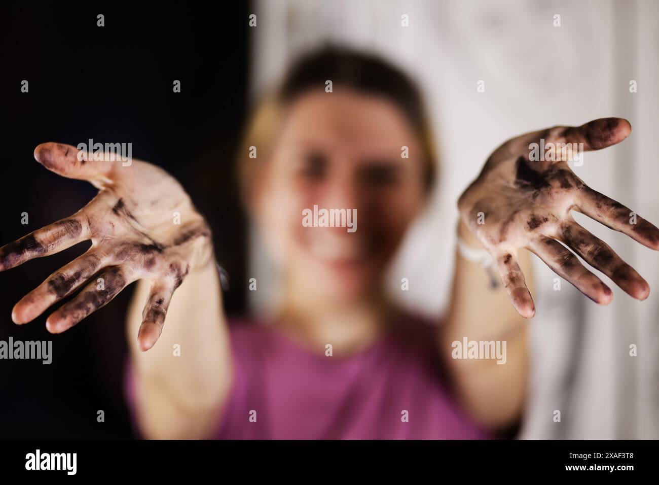 A joyful female artist stretches out her paint-covered hands, capturing ...