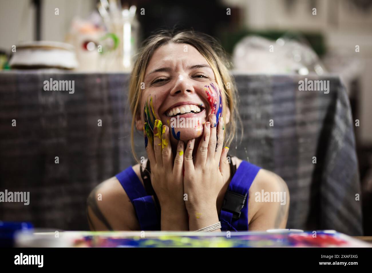 A young female artist expresses her joy in the art studio, covered in ...