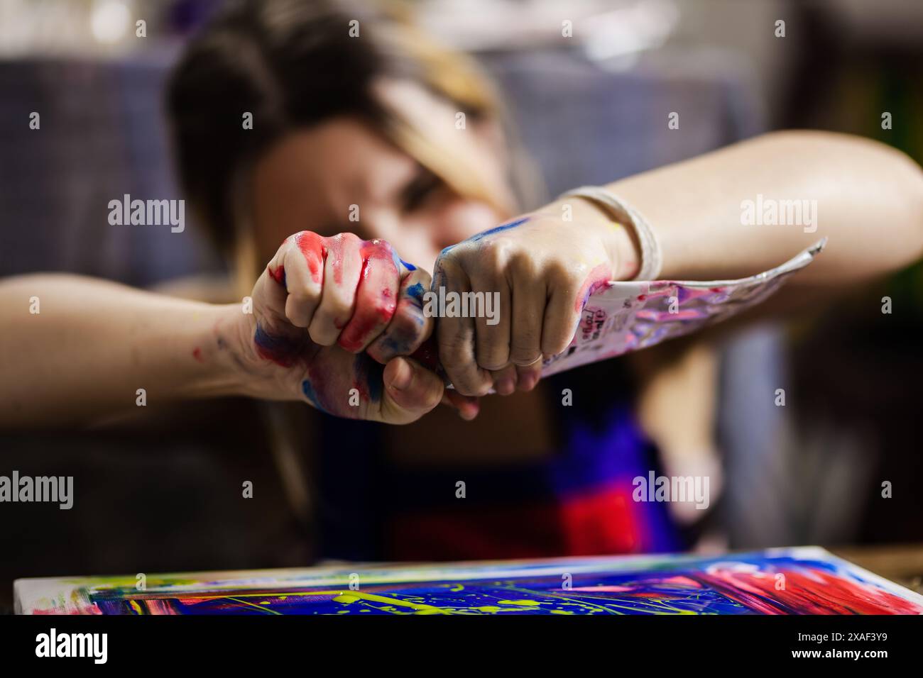 Focused female painter with paint-splattered hands works on a vibrant ...