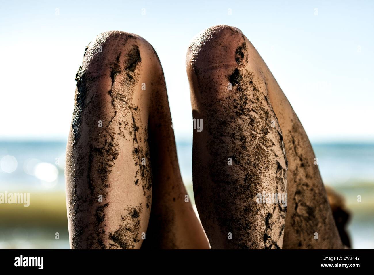 A close-up view of sandy legs against the backdrop of a bright blue sea ...