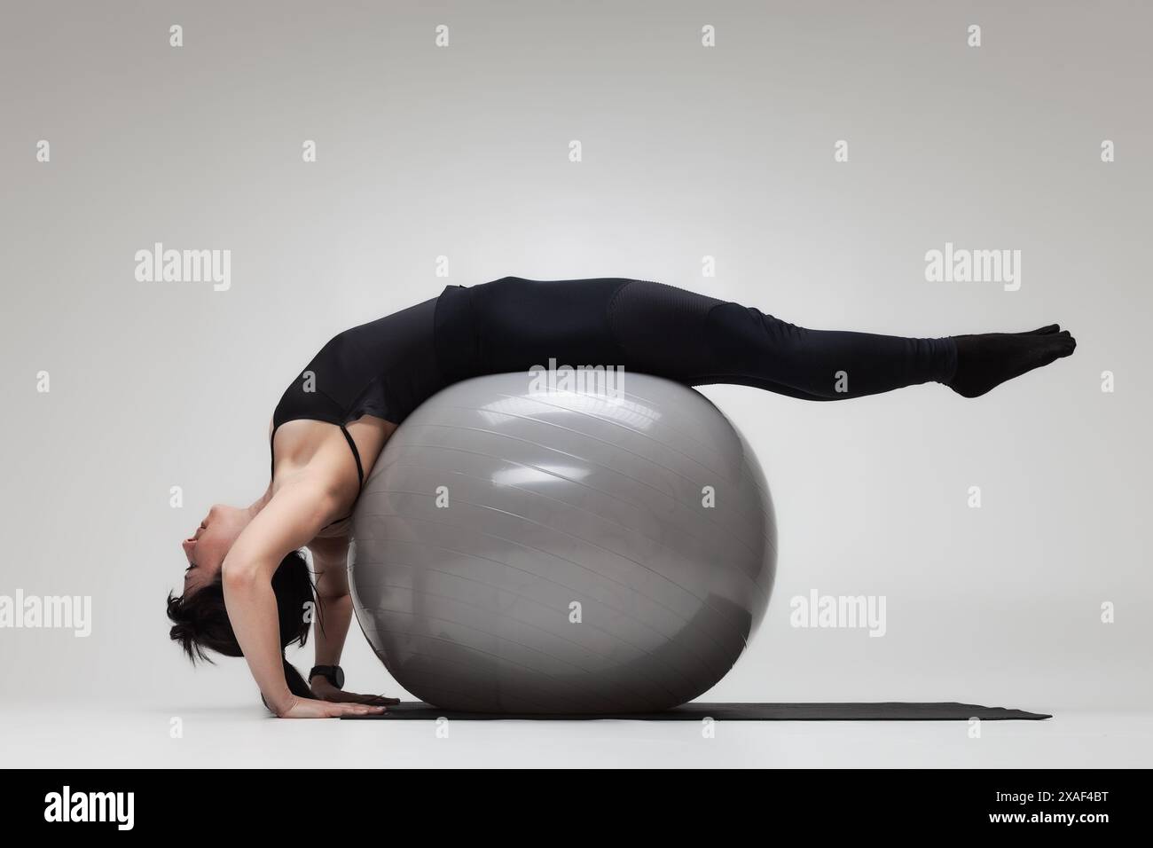 A focused young woman in black sportswear demonstrates flexibility and ...