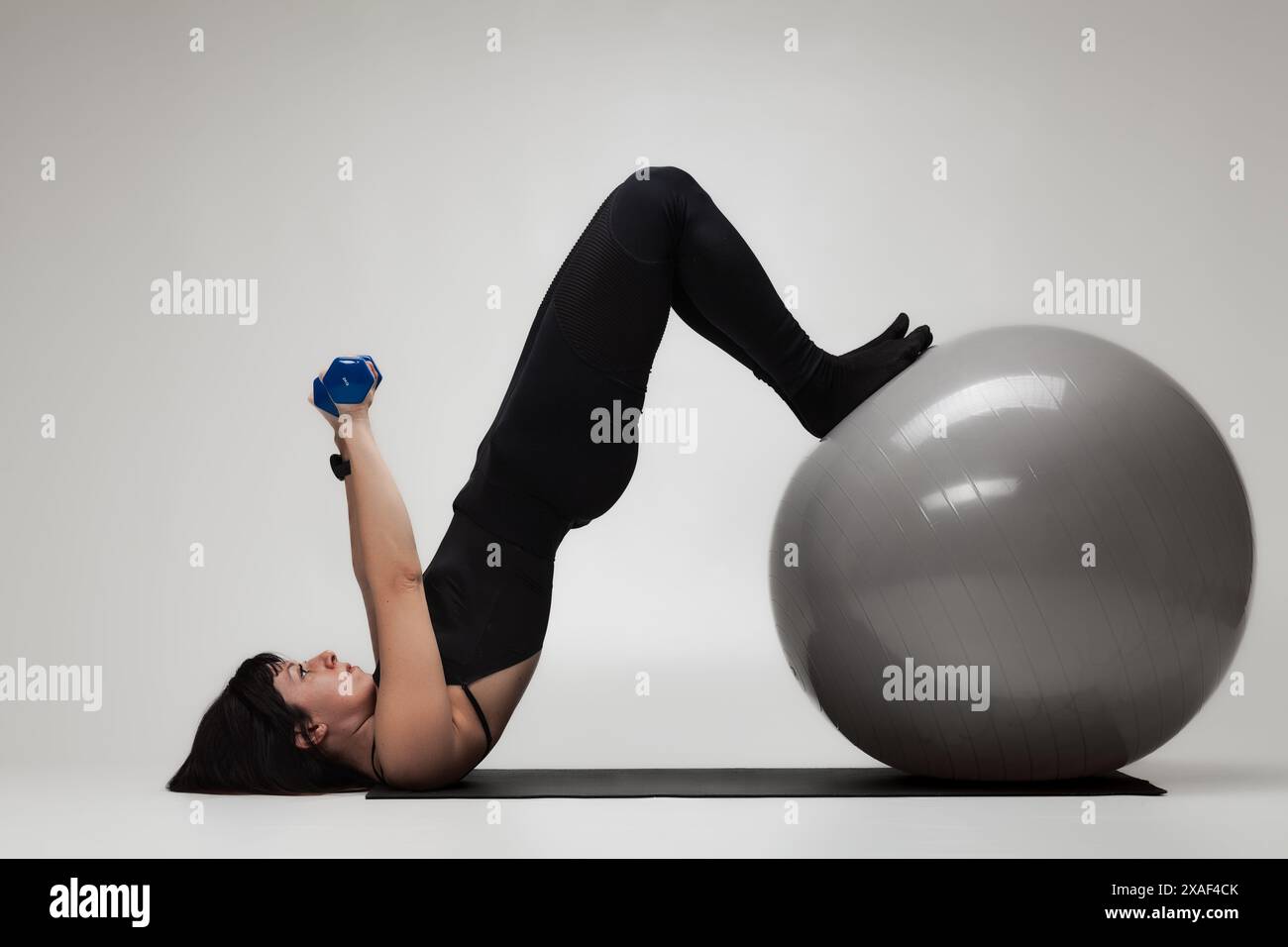 A young woman utilizing a gym exercise ball and a blue dumbbell for an ...