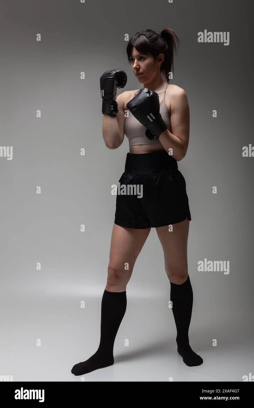 A young woman wearing black boxing gloves stands ready to train ...