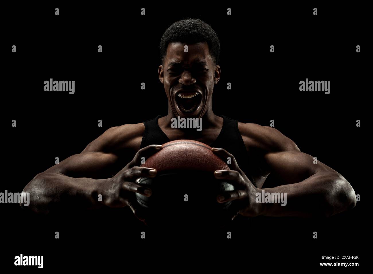 Basketball player holding a ball against black background. Screaming ...