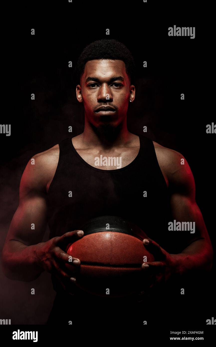 Basketball player side lit with red color holding a ball against black ...