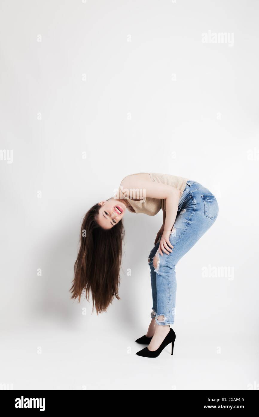 A playful young woman bends forward in ripped blue jeans and high heels ...