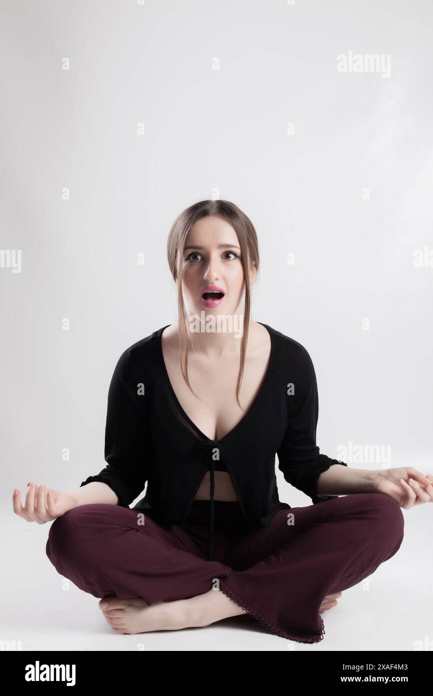 A young female adult seats in a lotus pose on a white background ...