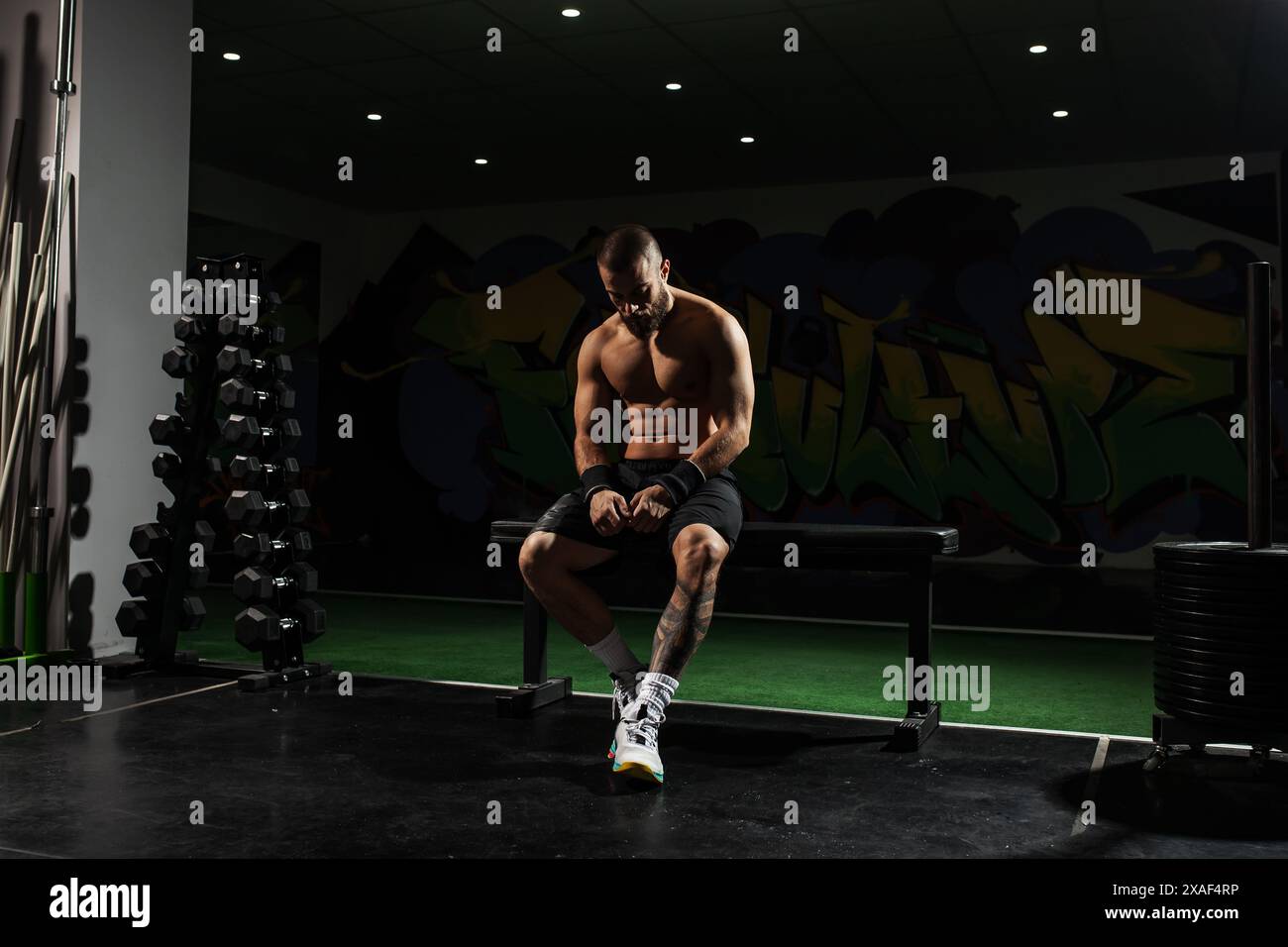 Focused muscular man sits contemplatively in a dimly lit gym with ...