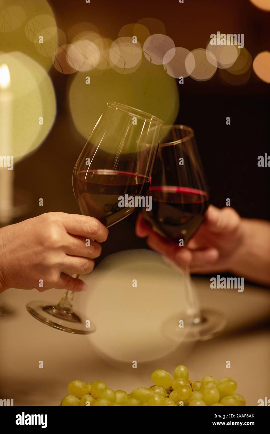 Vertical closeup of couple clinking wine glasses over table enjoying ...
