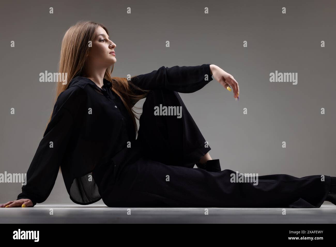 Confident young woman sitting on the floor in a casual, black outfit ...