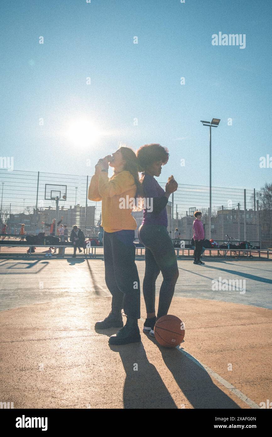 Group of teenagers sitting outside on a basketball field with stands ...