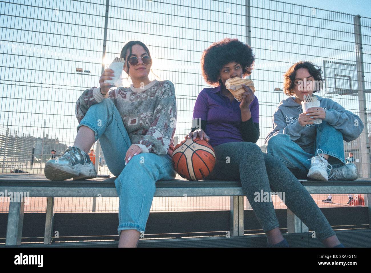 Group of teenagers sitting outside on a basketball field with stands ...
