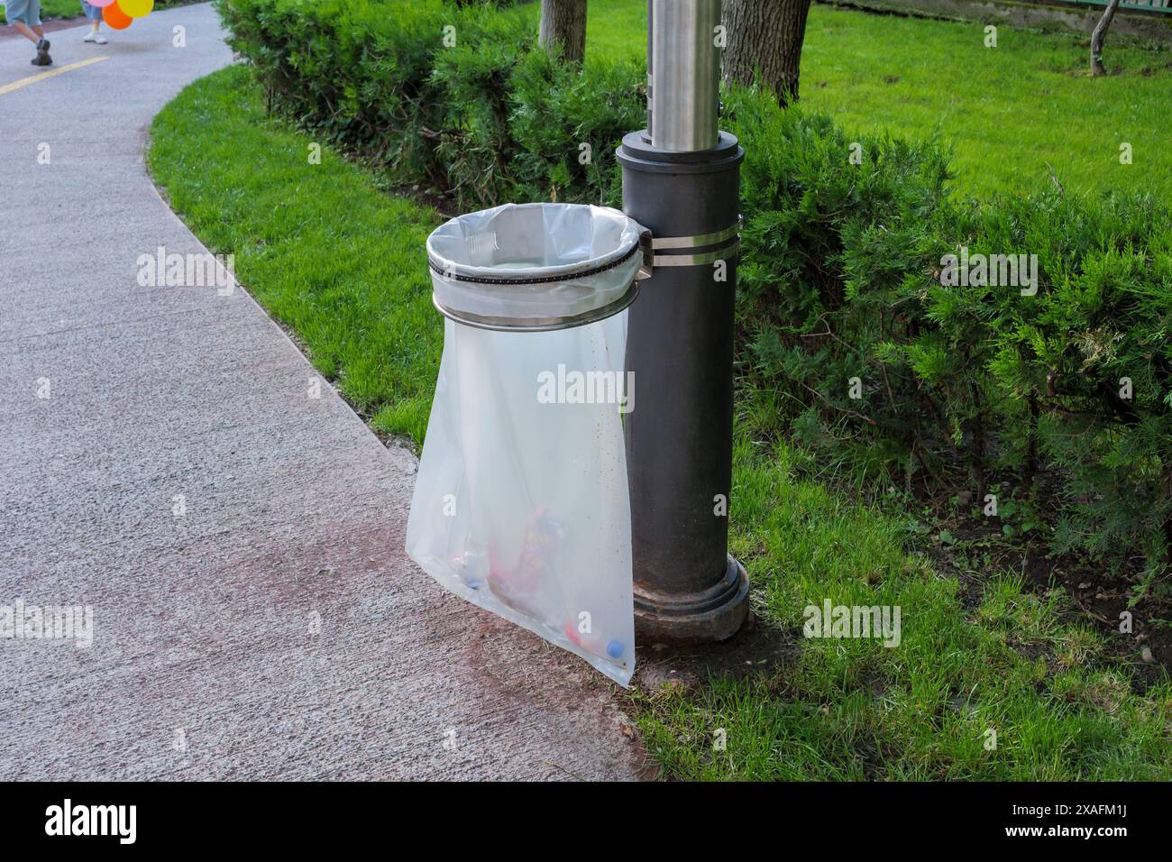 A plastic trash bag with garbage inside is attached to a lamppost along ...