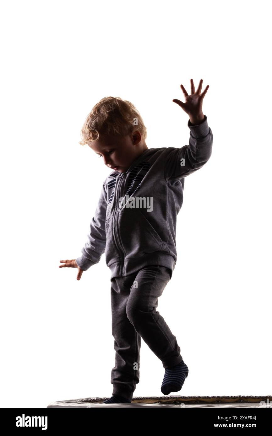 Silhouette of a young child in a grey outfit balancing on a trampoline ...