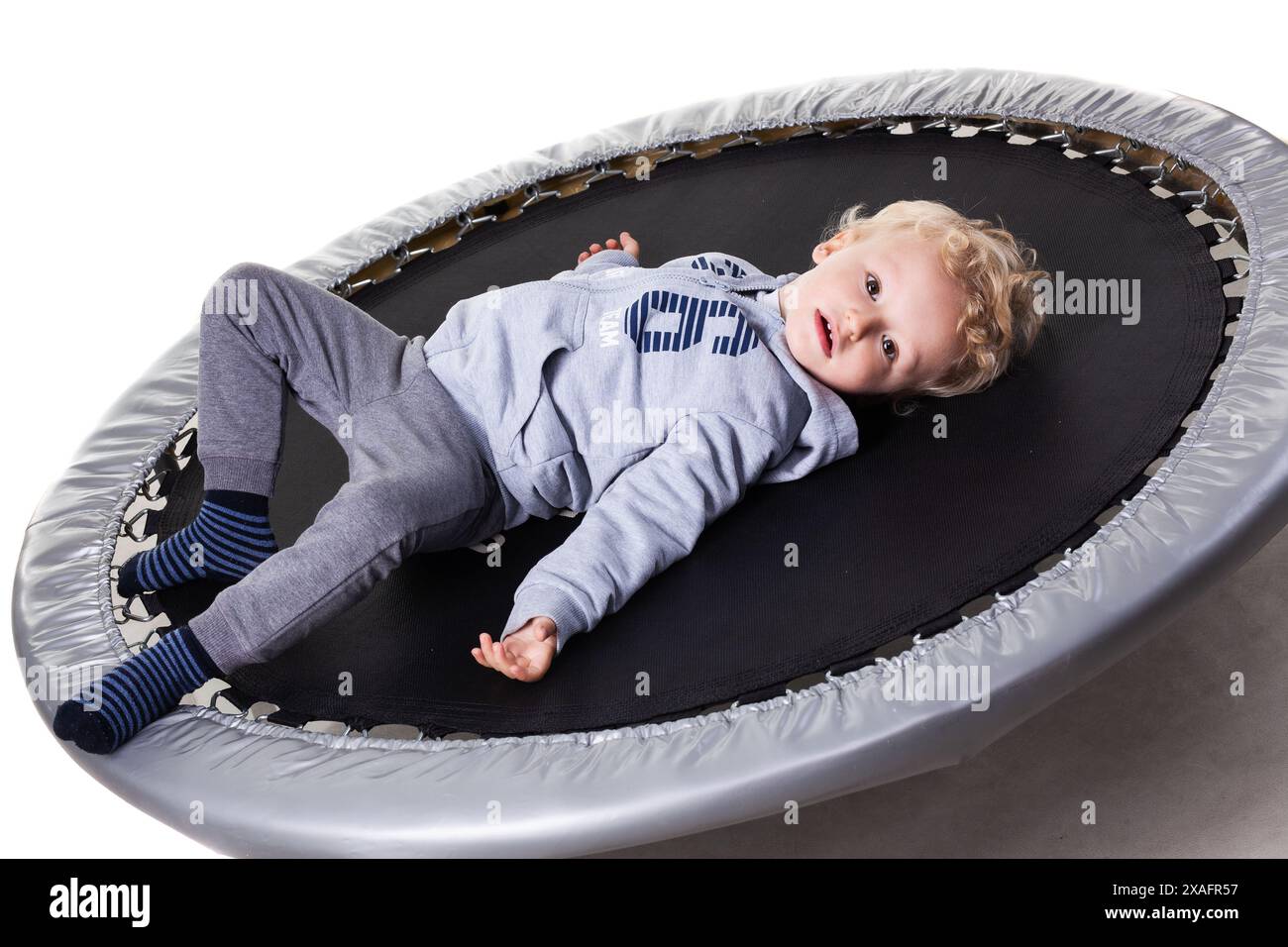 Adorable young child wearing grey clothes lying on a trampoline ...