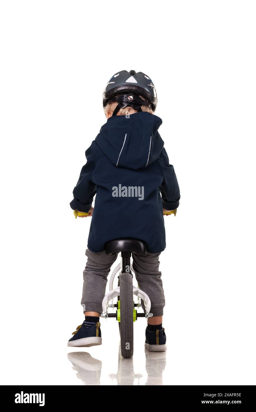 Rear view of a toddler riding a balance bike with a helmet, promoting ...