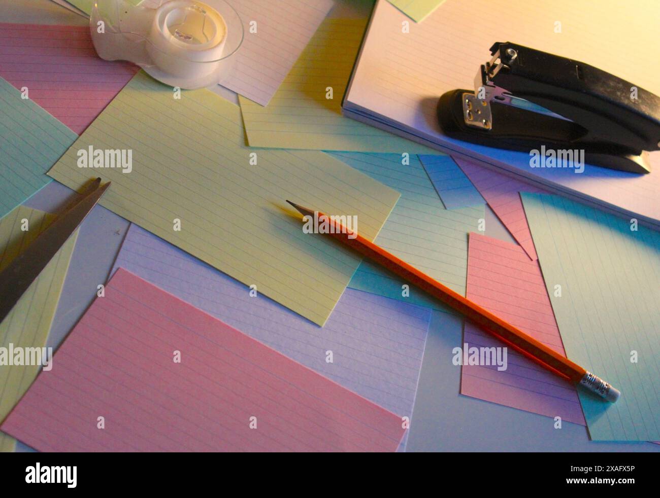A white, clustered and busy work desk with staplers, paper, flashcards ...