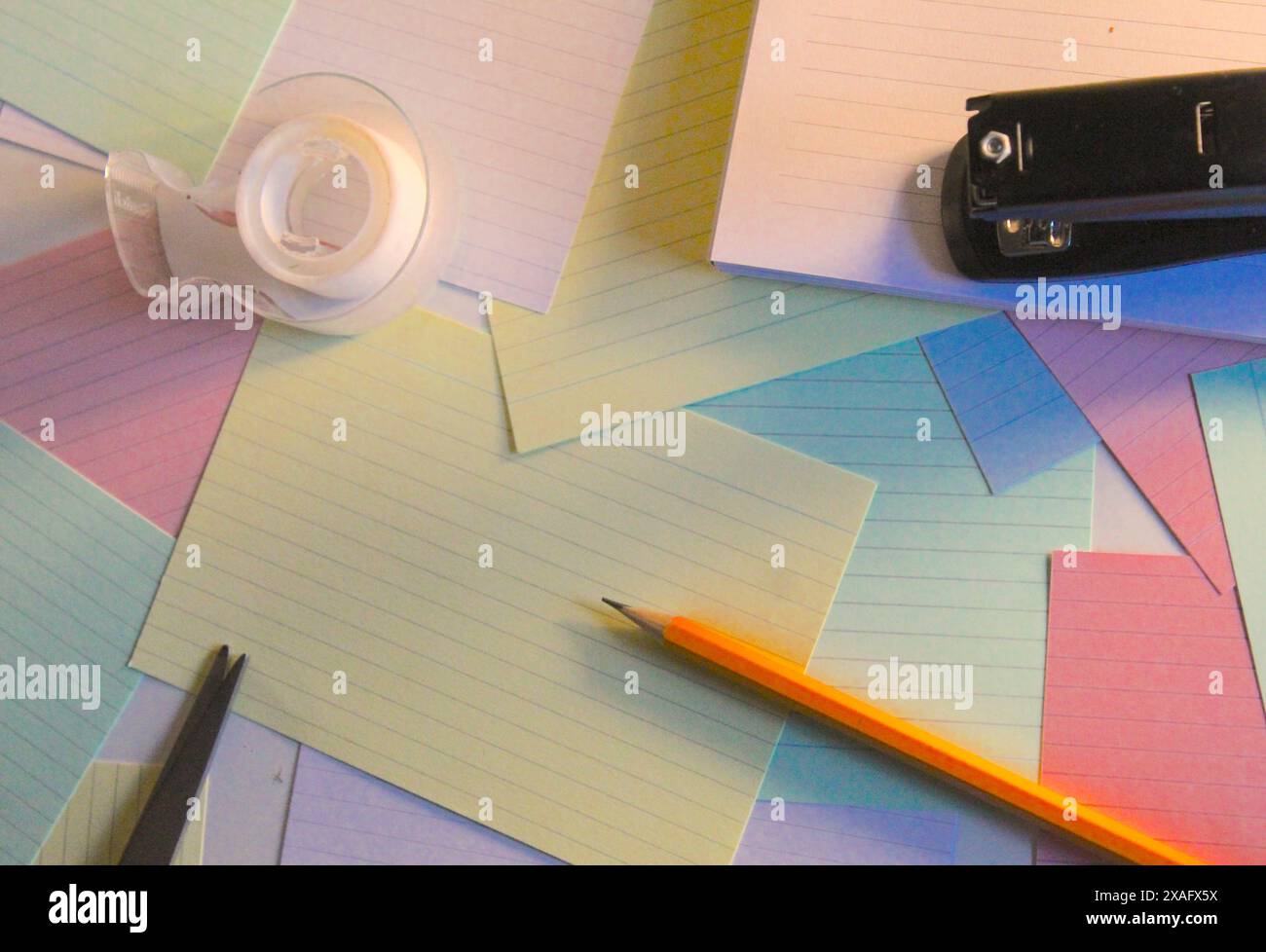 A white, clustered and busy work desk with staplers, paper, flashcards and pencils in a work ...
