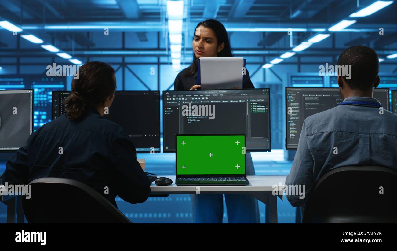 Multiethnic engineers working in high tech server hub, using green screen laptop and PCs to ...
