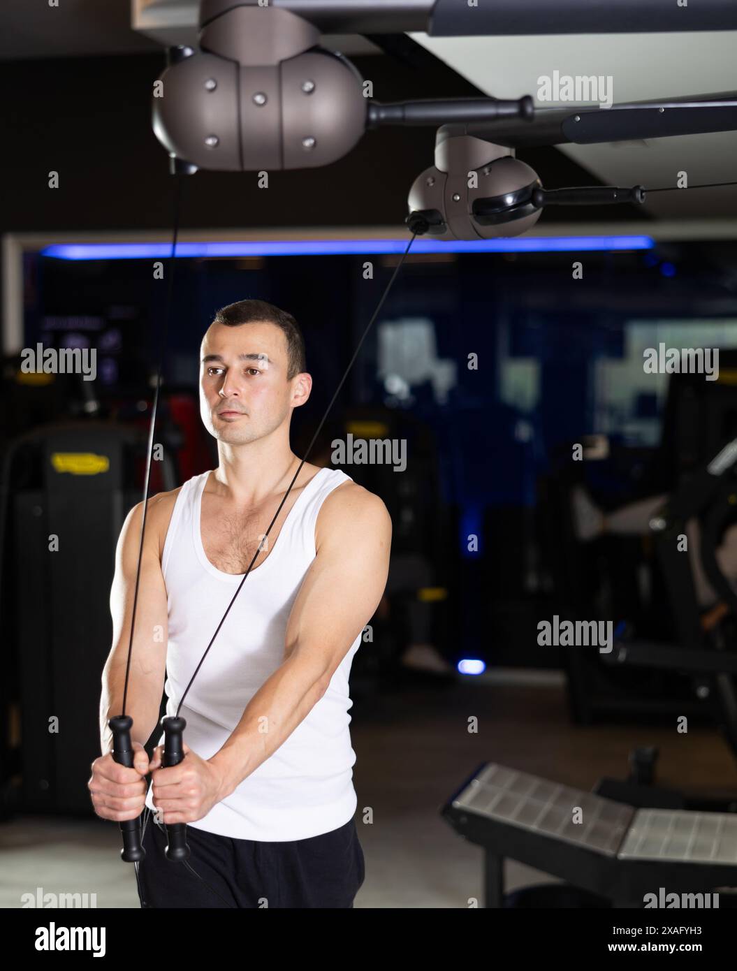 Sportive young guy training his arms on adjustable cable exercise ...