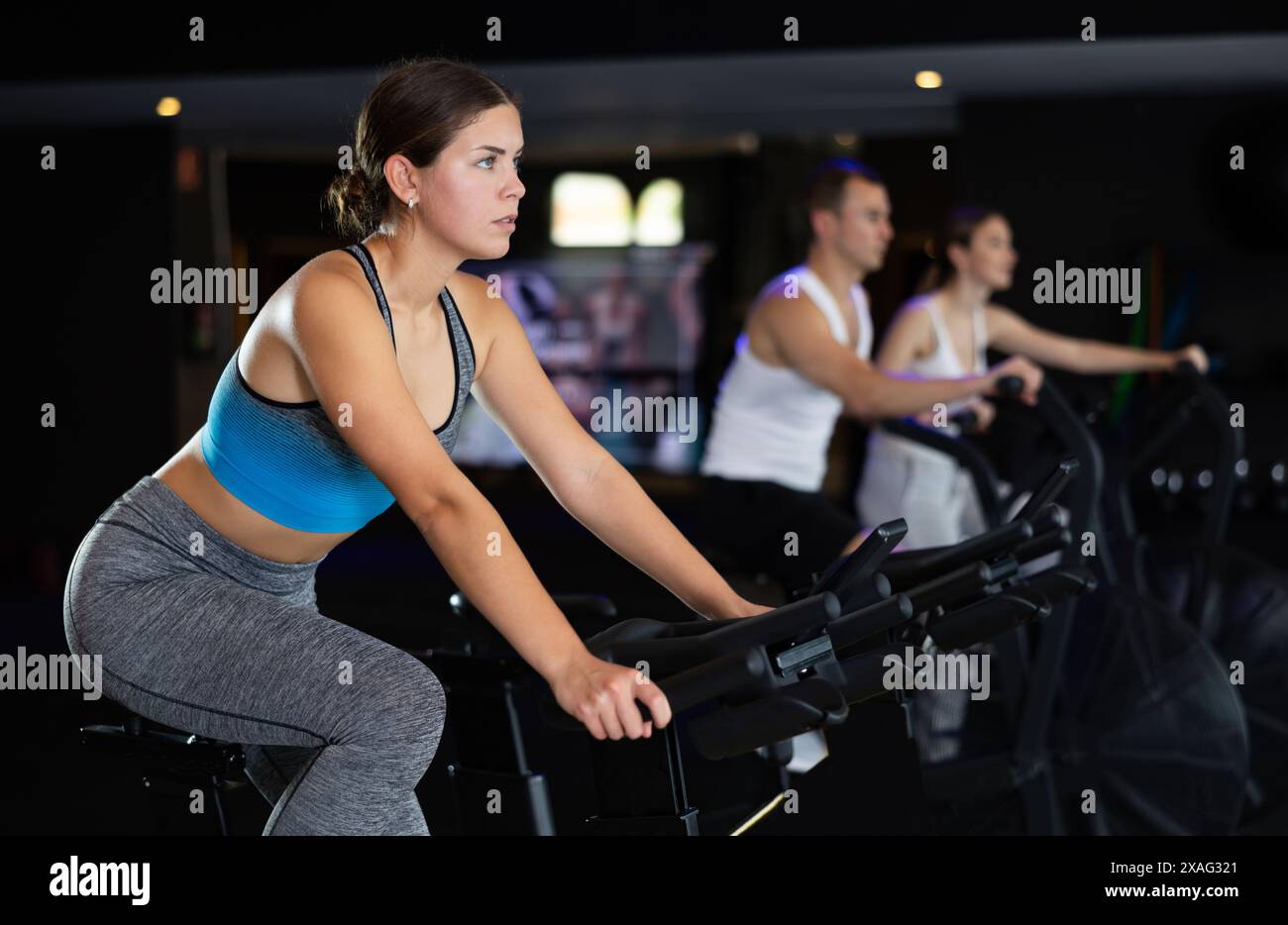 Sportive young girl doing spin bike exercises in well-equipped gym ...