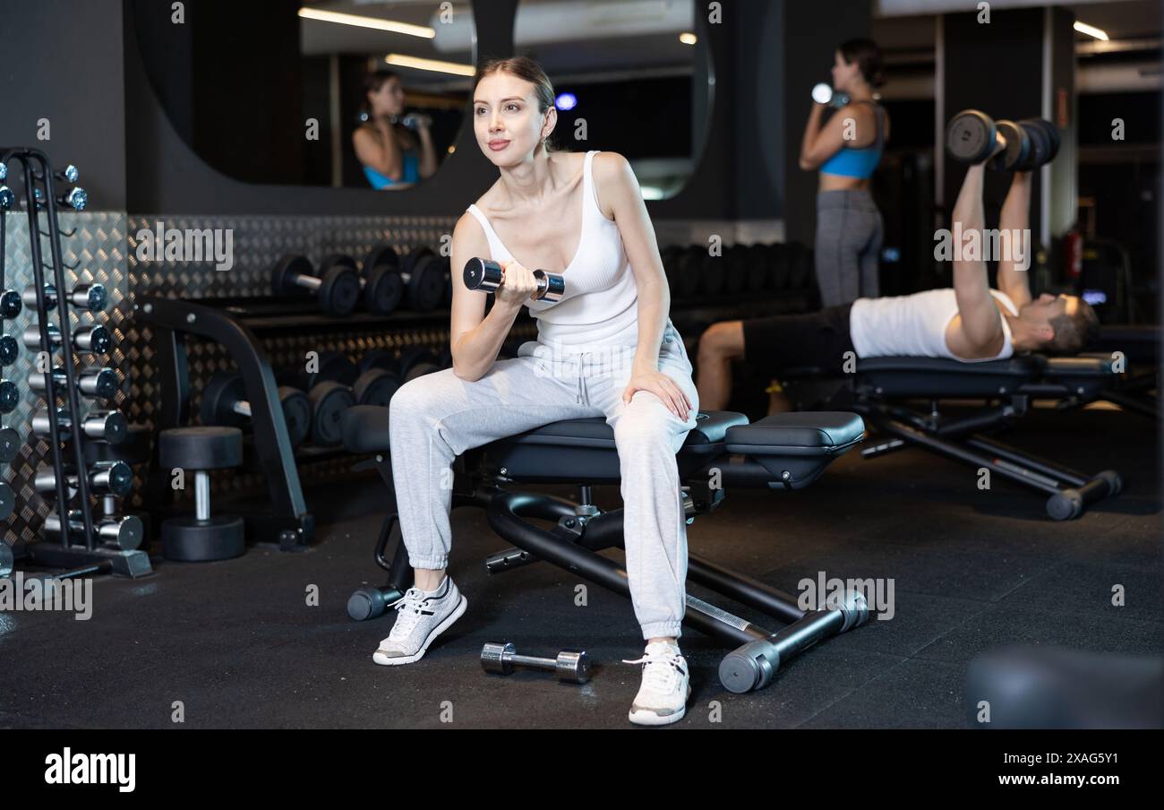 Slender girl trains muscles of arms and back using dumb-bell shaped ...