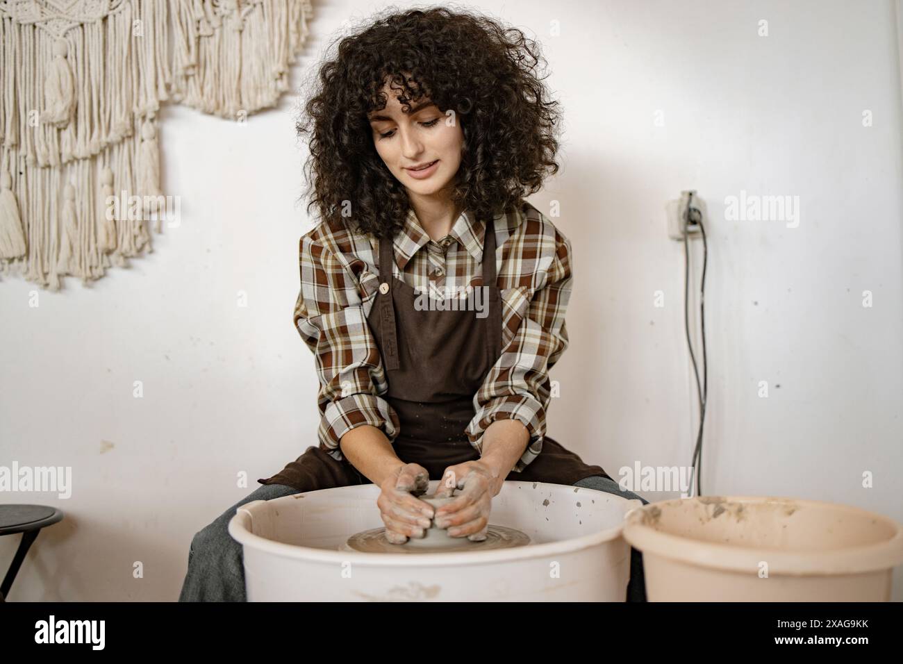 Young adult female potter using a pottery wheel to sculpt ceramic ...