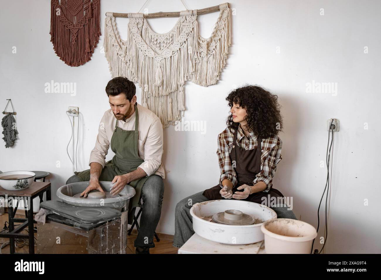 Man and woman potter creating clay vase together on potter's wheel in ...
