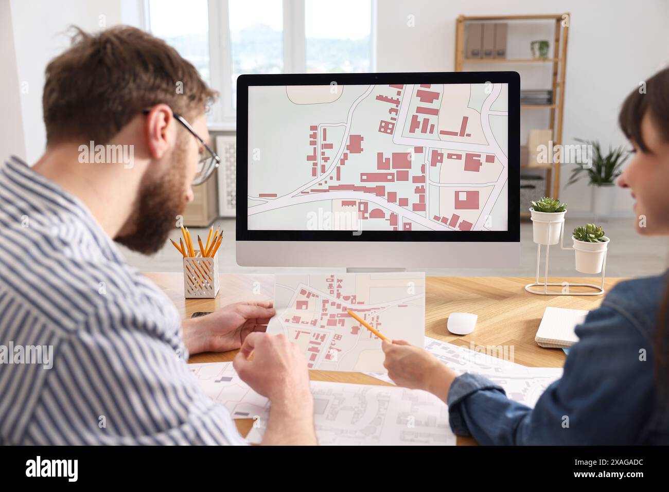 Cartographers working with cadastral maps at table in office, back view ...