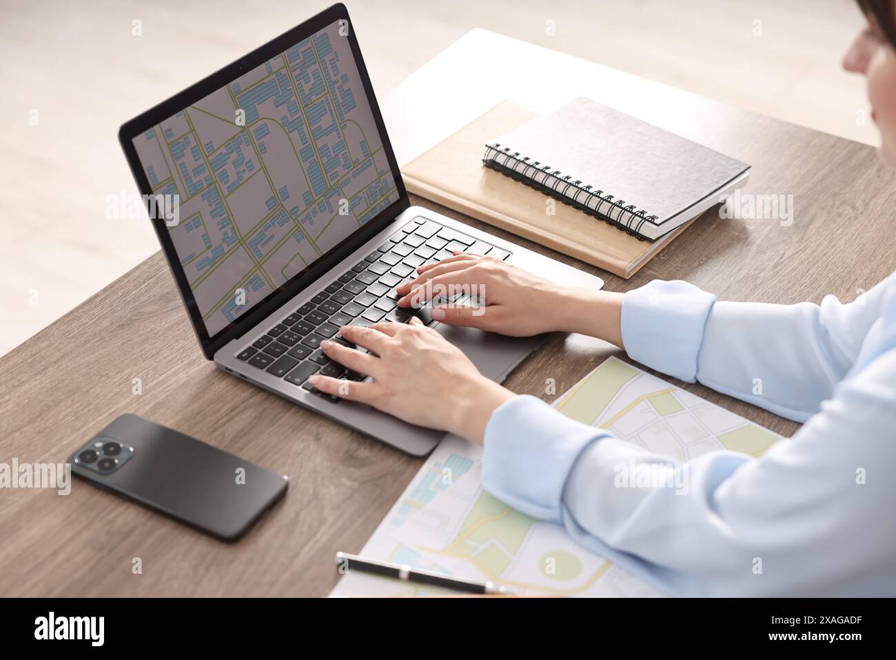 Cartographer working with cadastral map on laptop at wooden table in ...