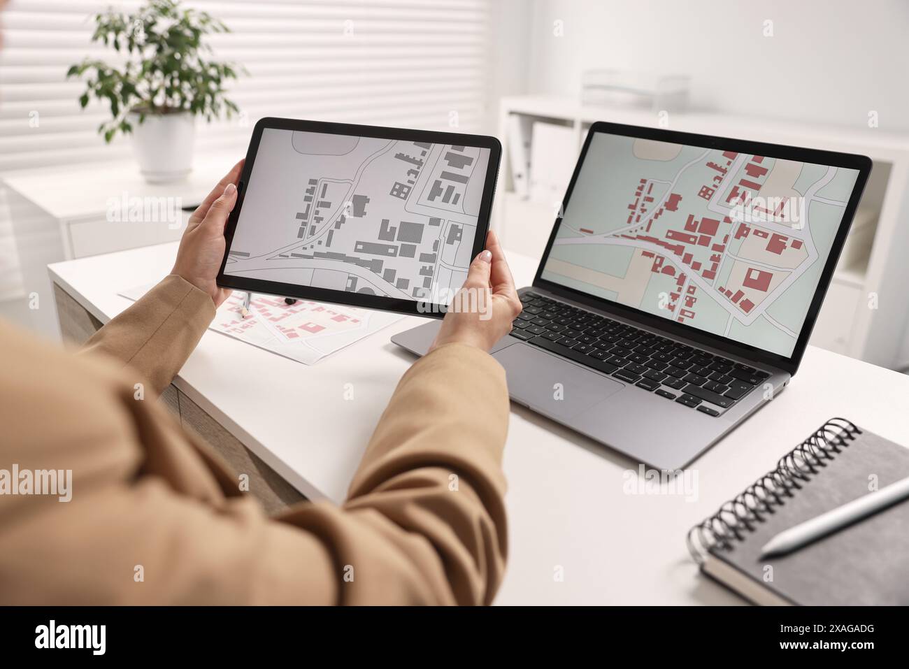 Cartographer working with cadastral maps on devices at white table in ...