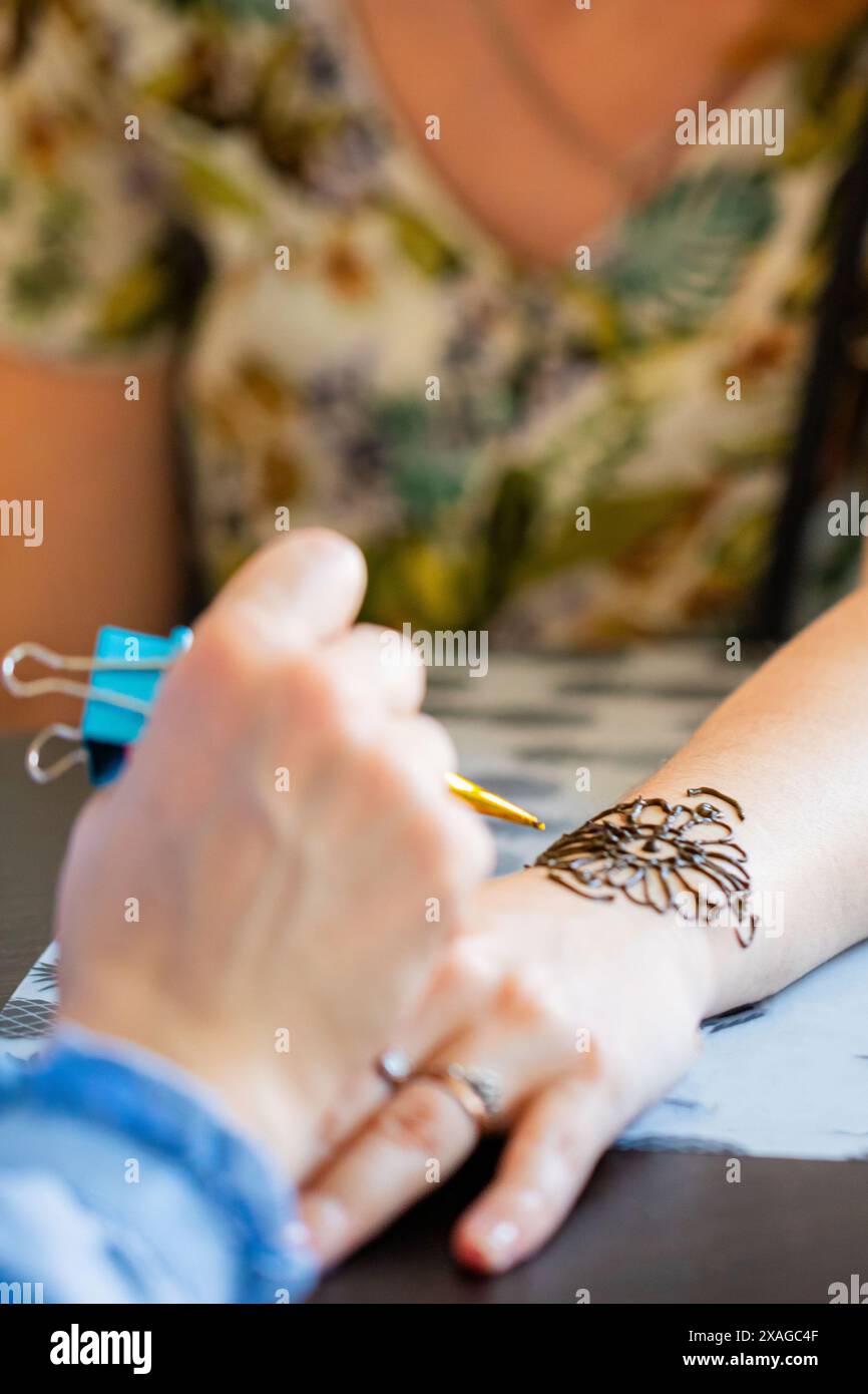 A woman is receiving a henna tattoo on her wrist at a salon. The artist ...