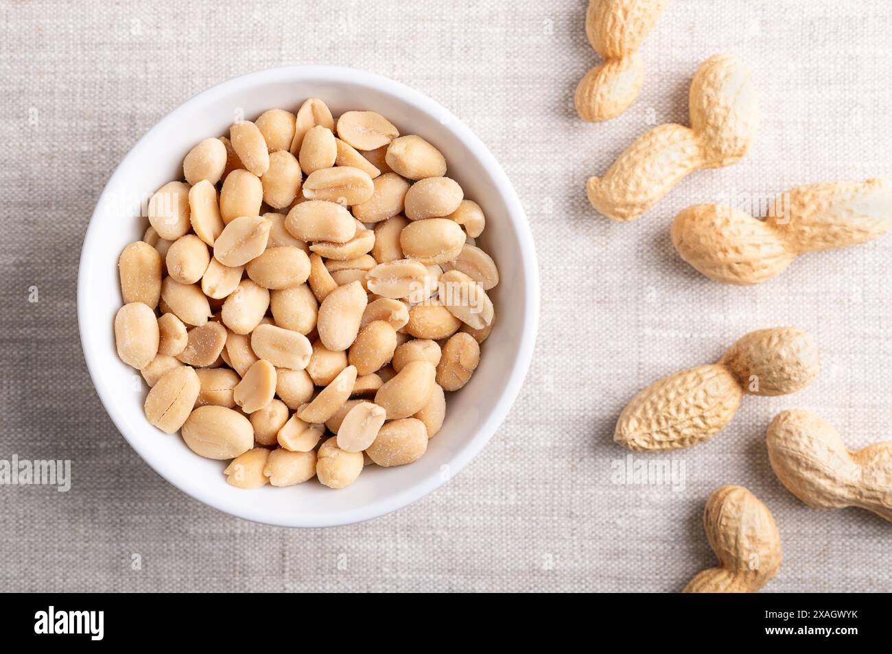 Roasted and salted peanuts in a white bowl on linen fabric. Ready-to ...