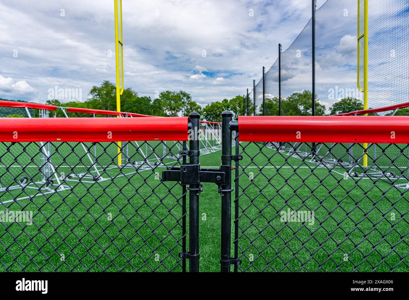 Black chain link fence, gate, with red fence cap and softball / baseball field in background ...