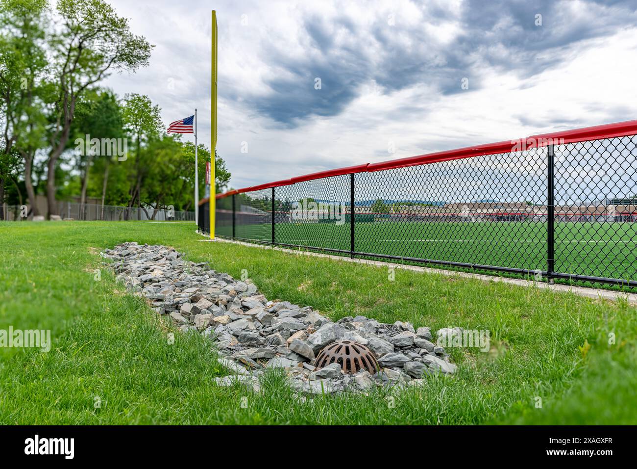 Black chain link fence with red fence cap and softball / baseball sports field in background ...
