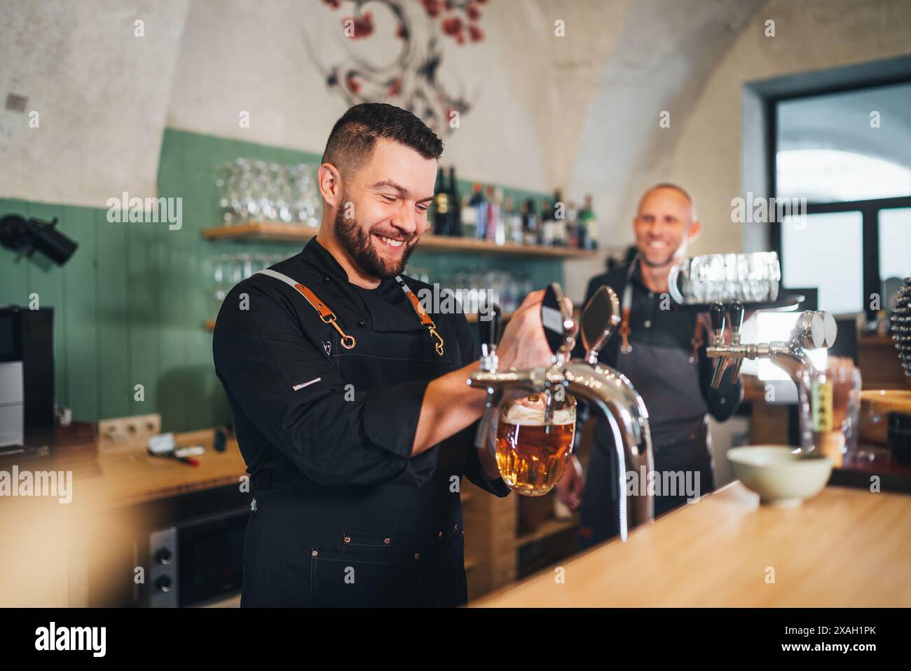Stylish bearded barman dressed black uniform smiling at camera, beer ...