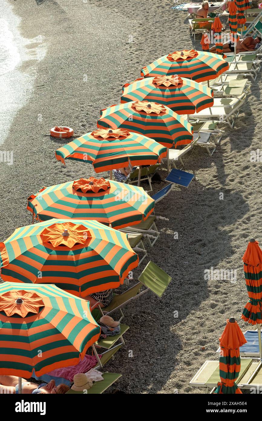 at Monterosso al Mare, Cinque Terre a single line orange and green beach umbrellas and sun ...