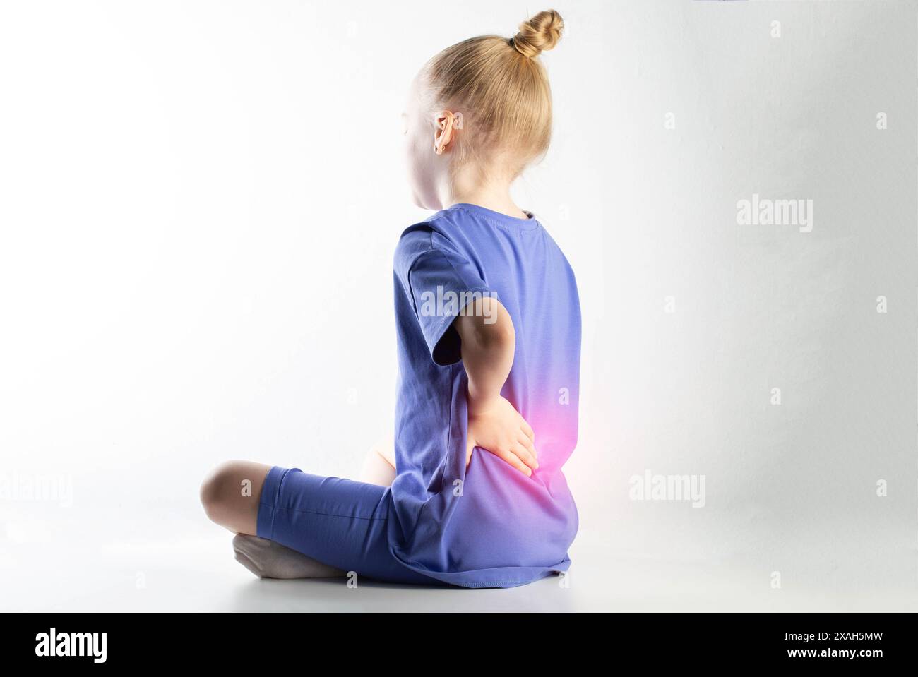 A girl in a purple suit sits and holds her lower back on a white ...