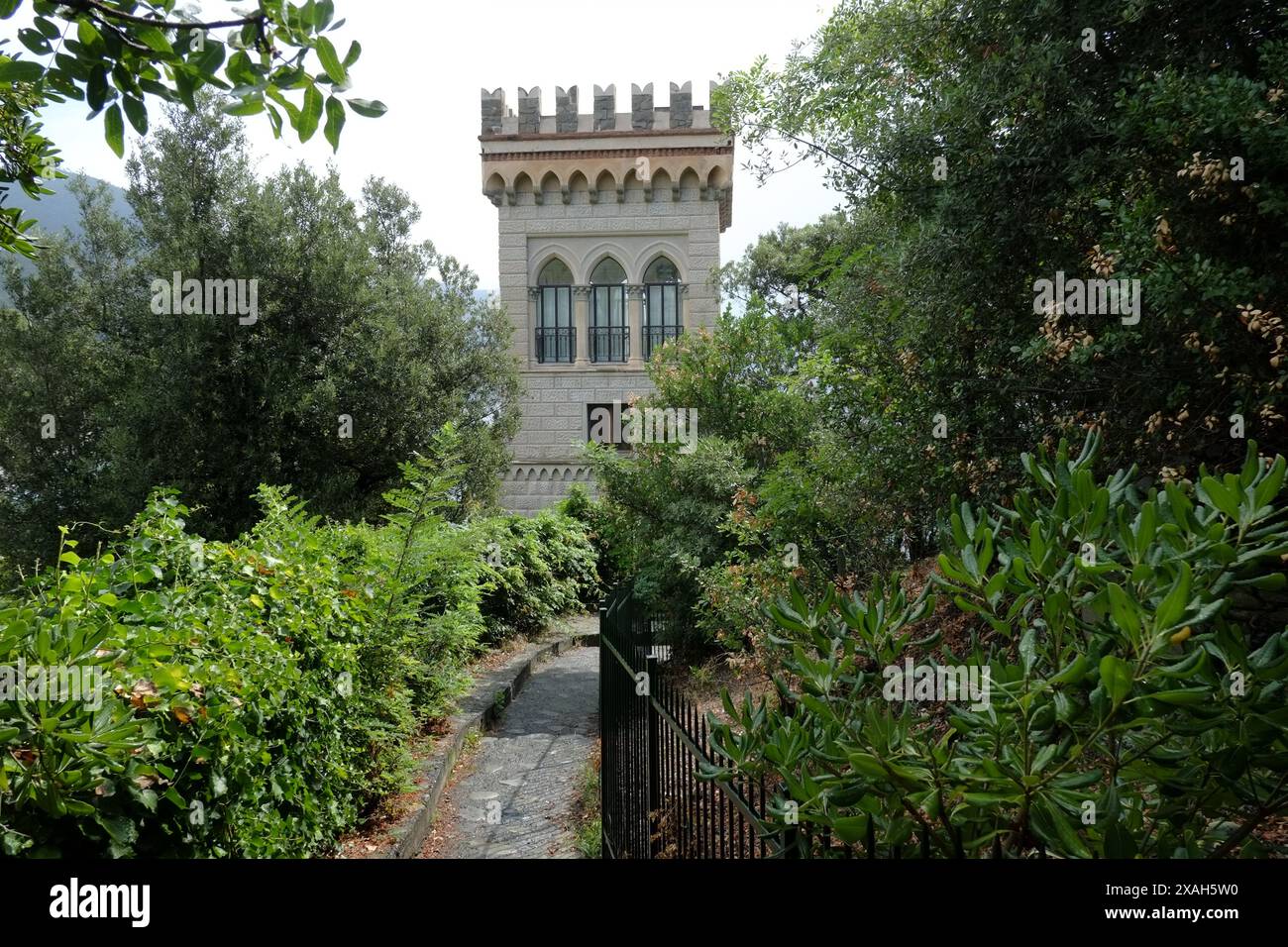 Garden path to a swallowtail battlement tower house with gothic arch ...