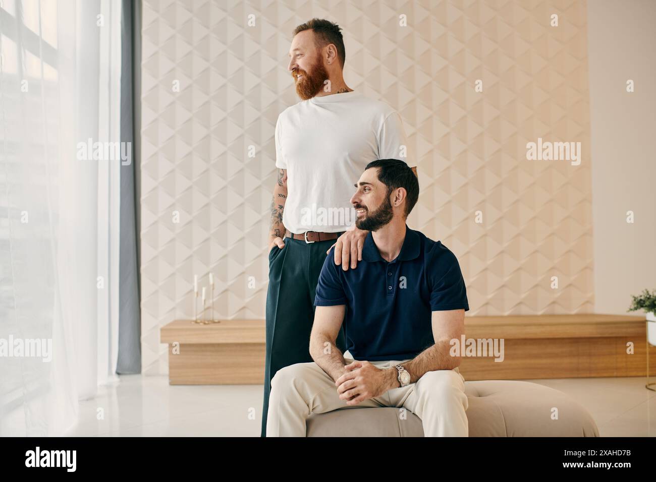 Two men in casual clothes sit on a couch in a modern living room ...