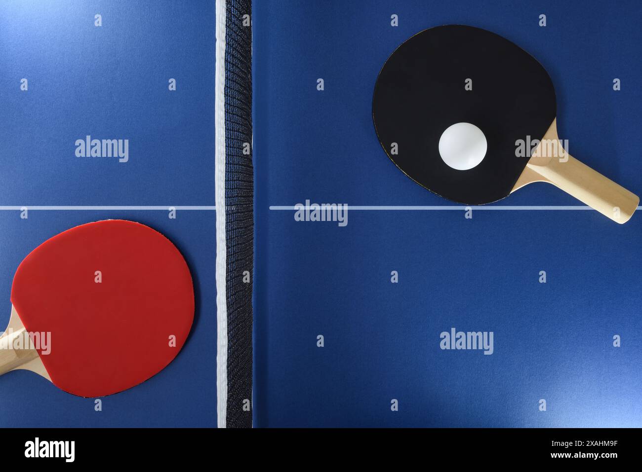 Table tennis paddles and white ball on blue game table with net. Top ...