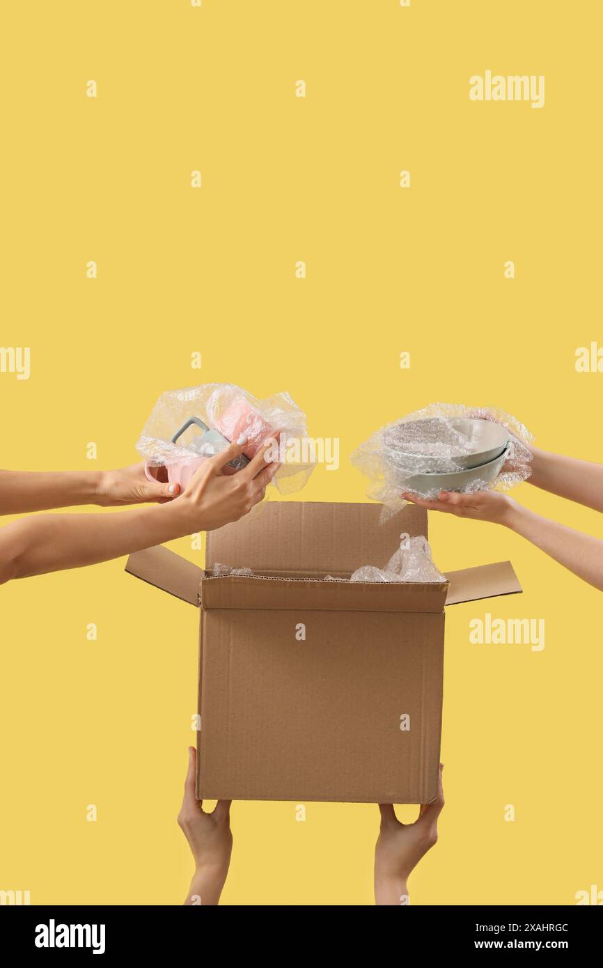 Women with moving box and wrapped dishes on yellow background Stock ...