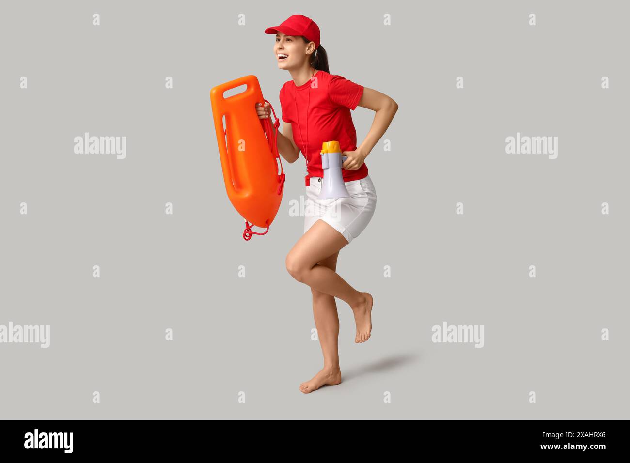Female lifeguard with rescue tube buoy and megaphone running on grey ...