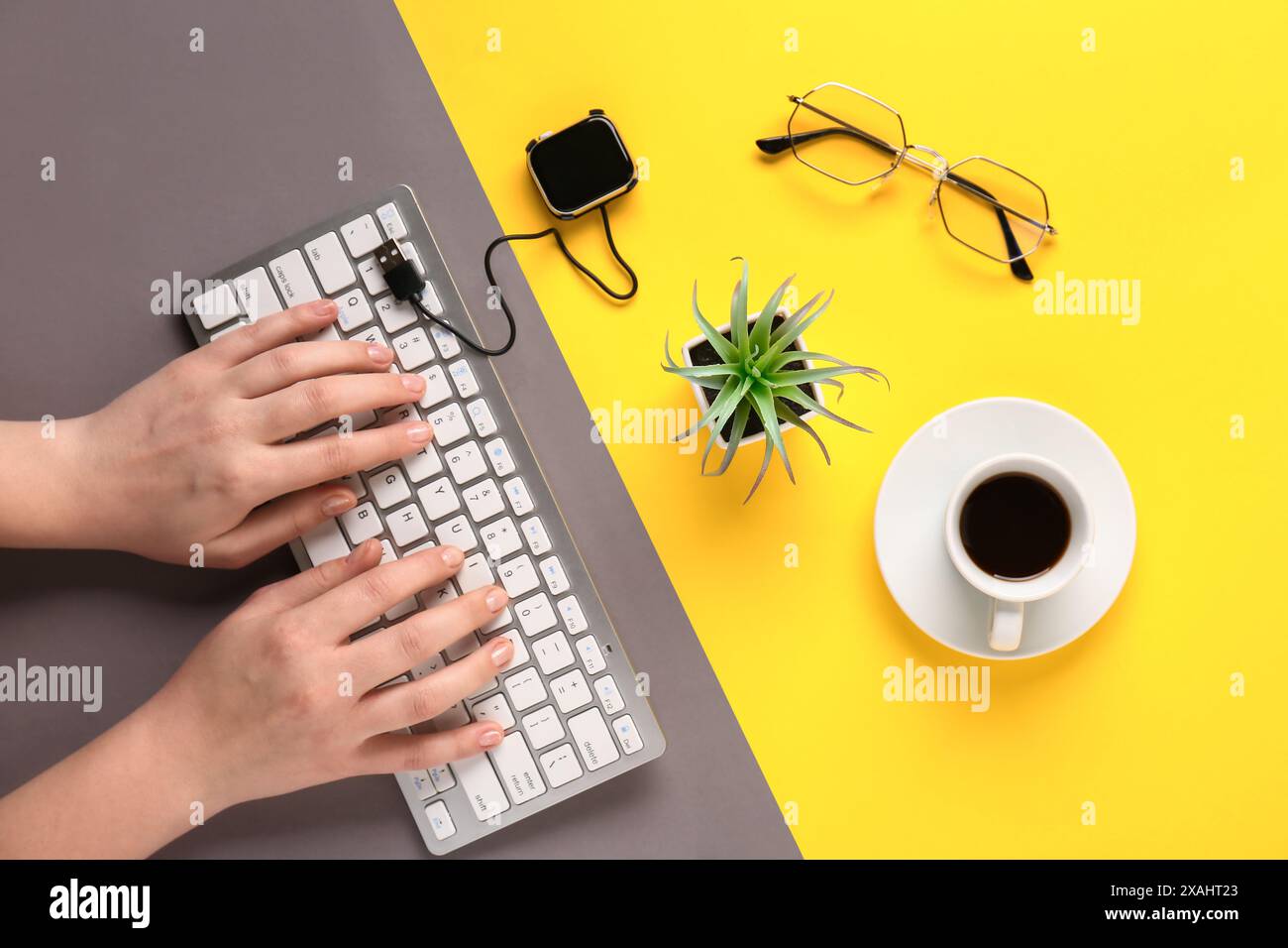 Female hands typing on keyboard on grey and yellow background. Top view ...