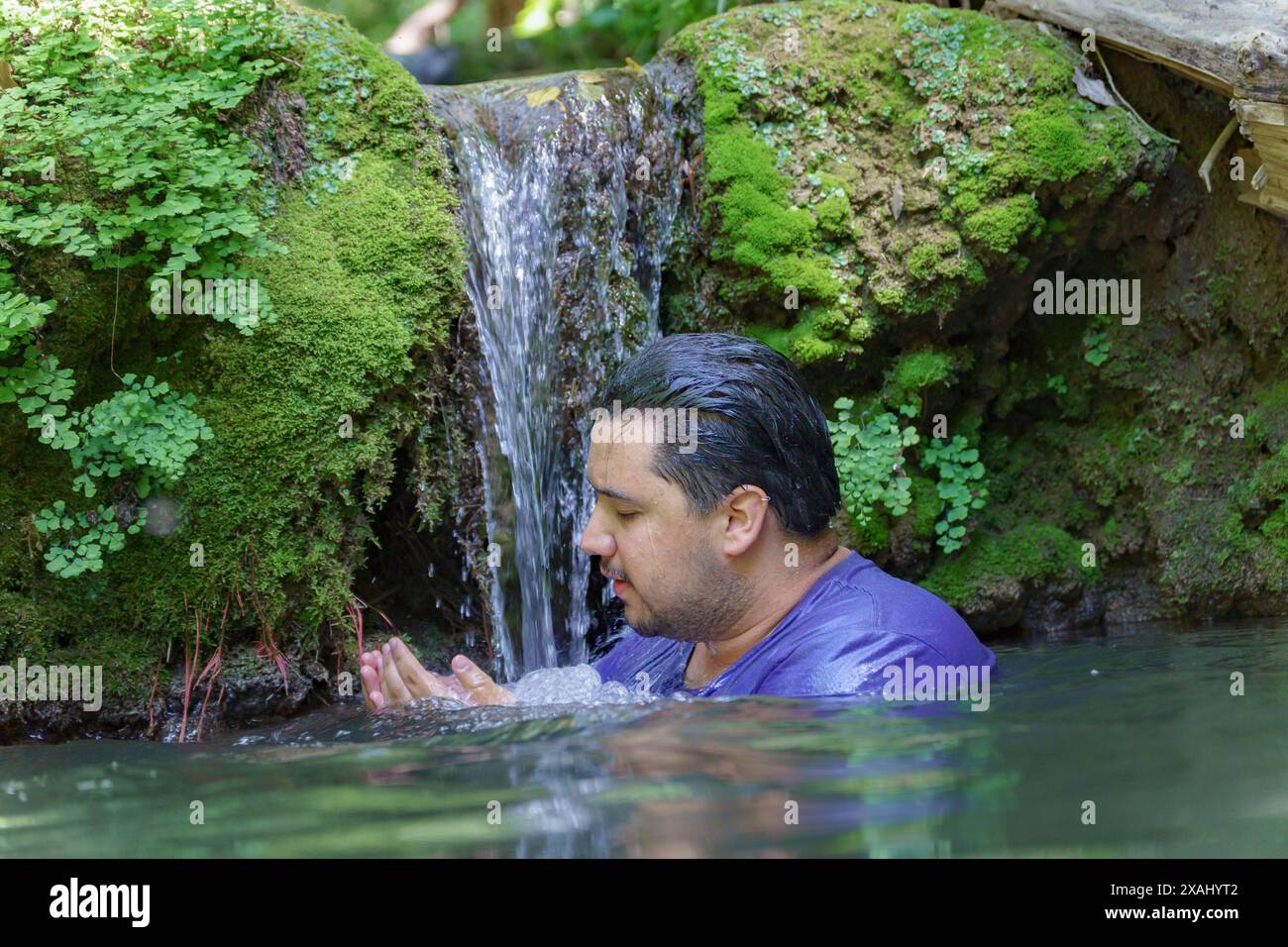 Attractive young dark-haired boy cooling off under the waterfall of a ...