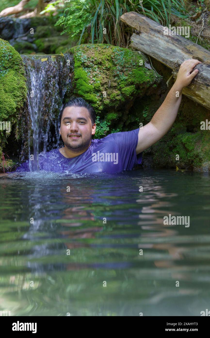 Attractive young dark-haired boy cooling off under the waterfall of a ...